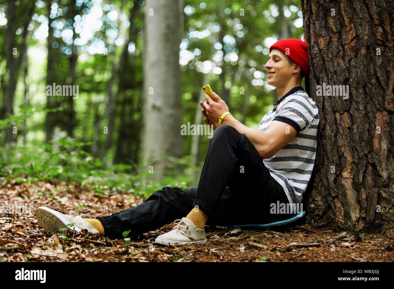 Young man wearing red hat sitting at the tree in nature forest during ...