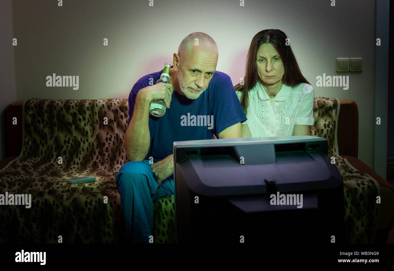 Middle-aged man and woman, watch television, looking sad, sitting on a ...