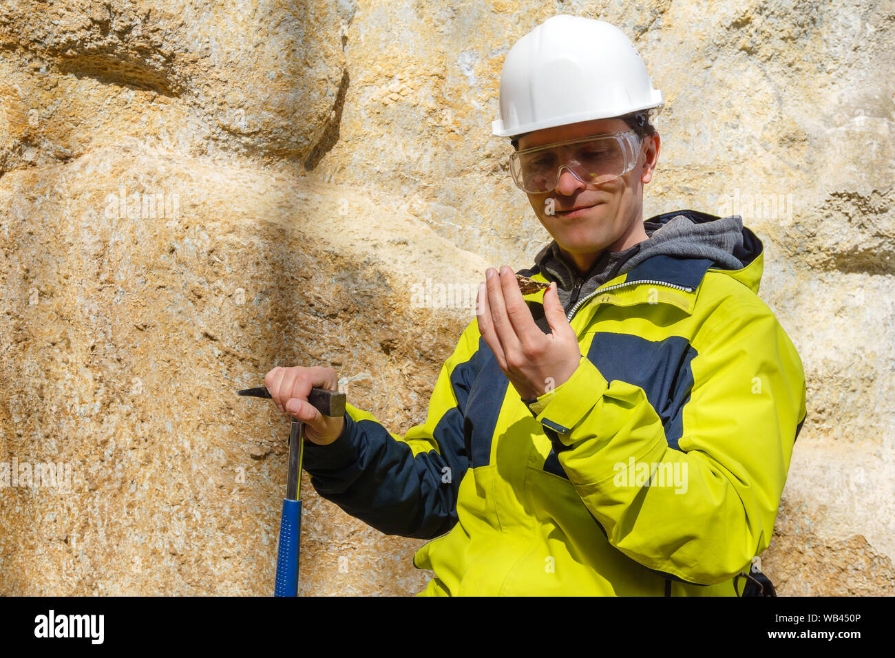 male geologist in helmet and protective glasses examines a sample of ...