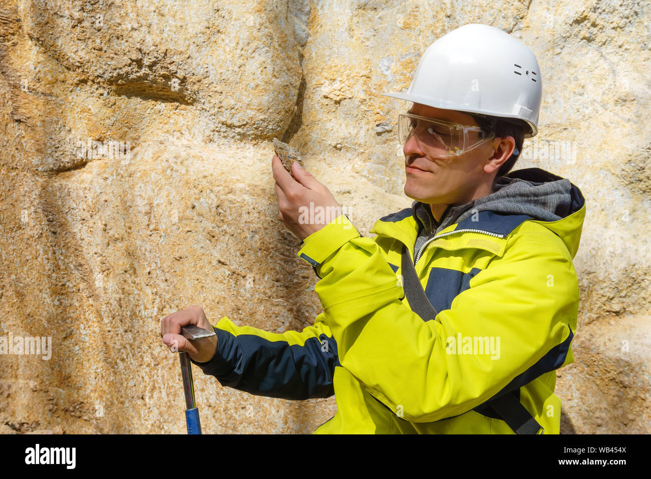 male geologist in helmet and protective glasses examines a sample of ...