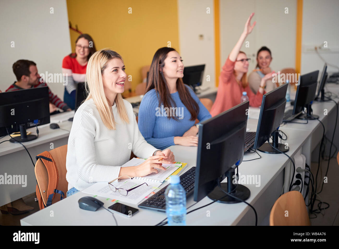 Smiling students sitting together at table using computer in class ...