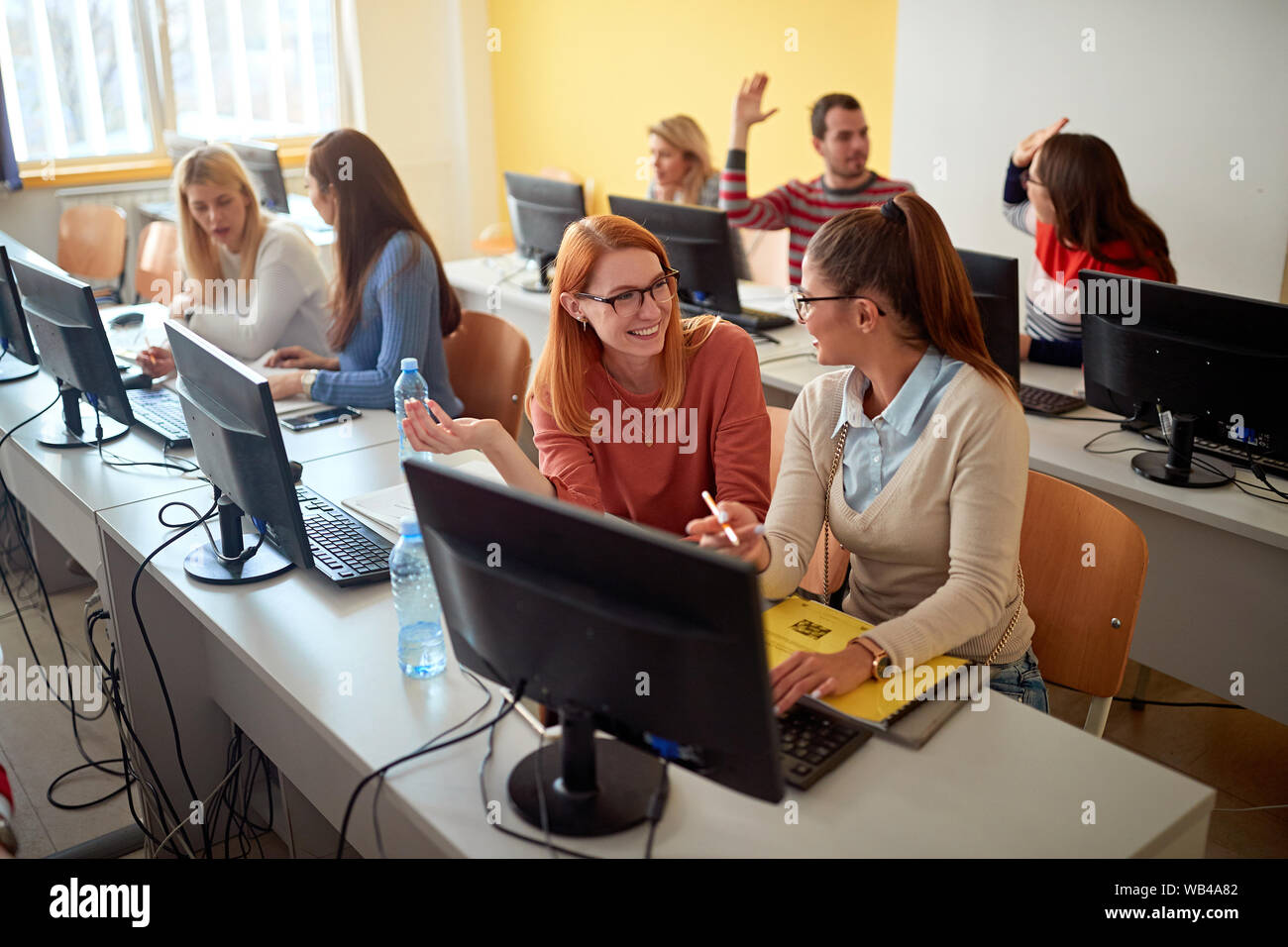 Group of smiling students sitting together at table using computer in ...