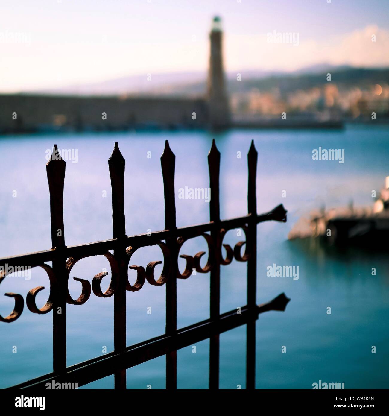 A wrought iron gate in the foreground with a lighthouse in the distance ...