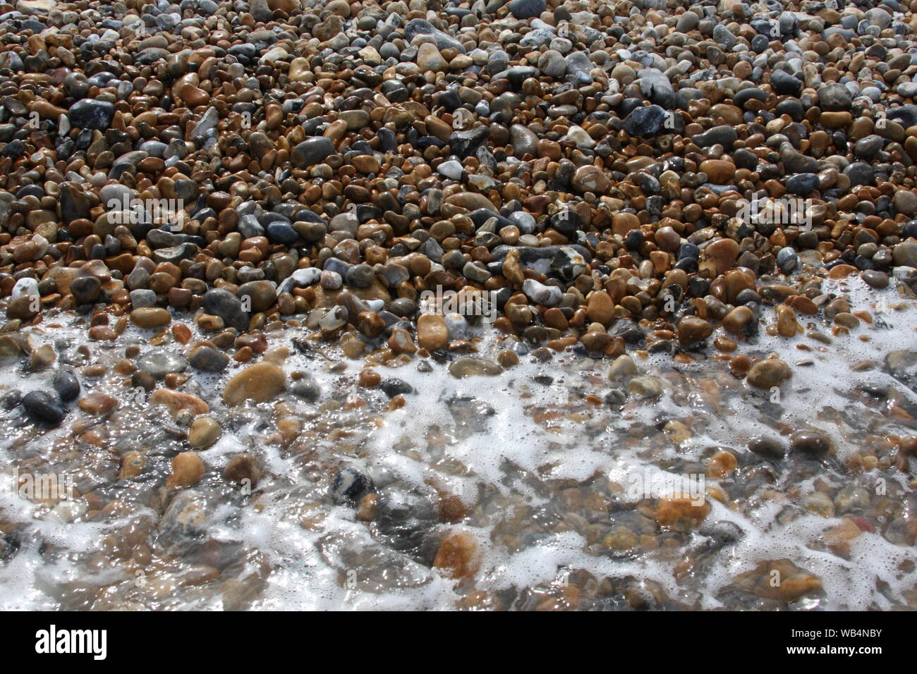 Shingle beach taken from sea with small wave washes over the pebbles ...