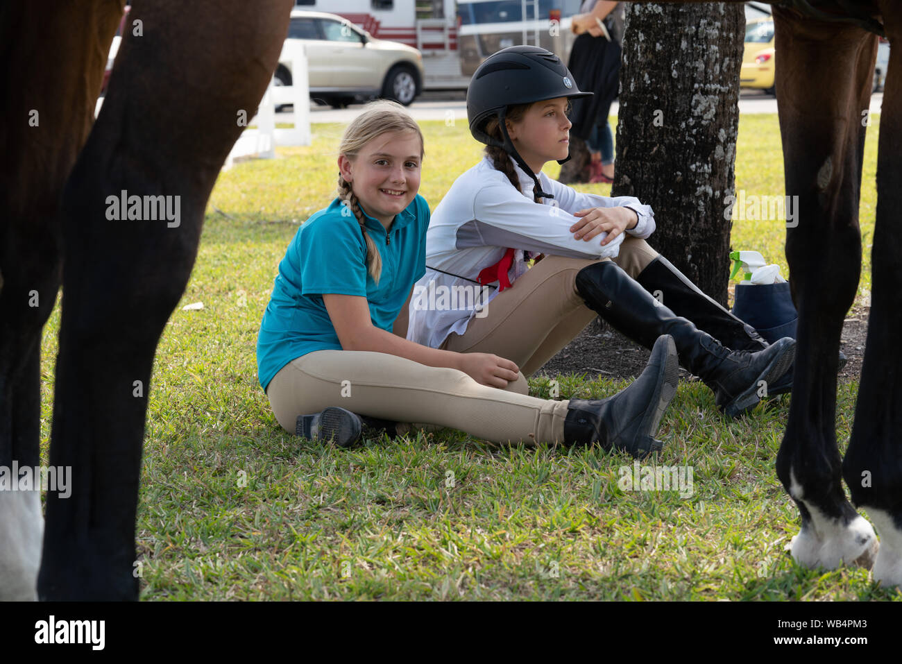 Two equestrian girls are sitting together on the grass next to a horse ...