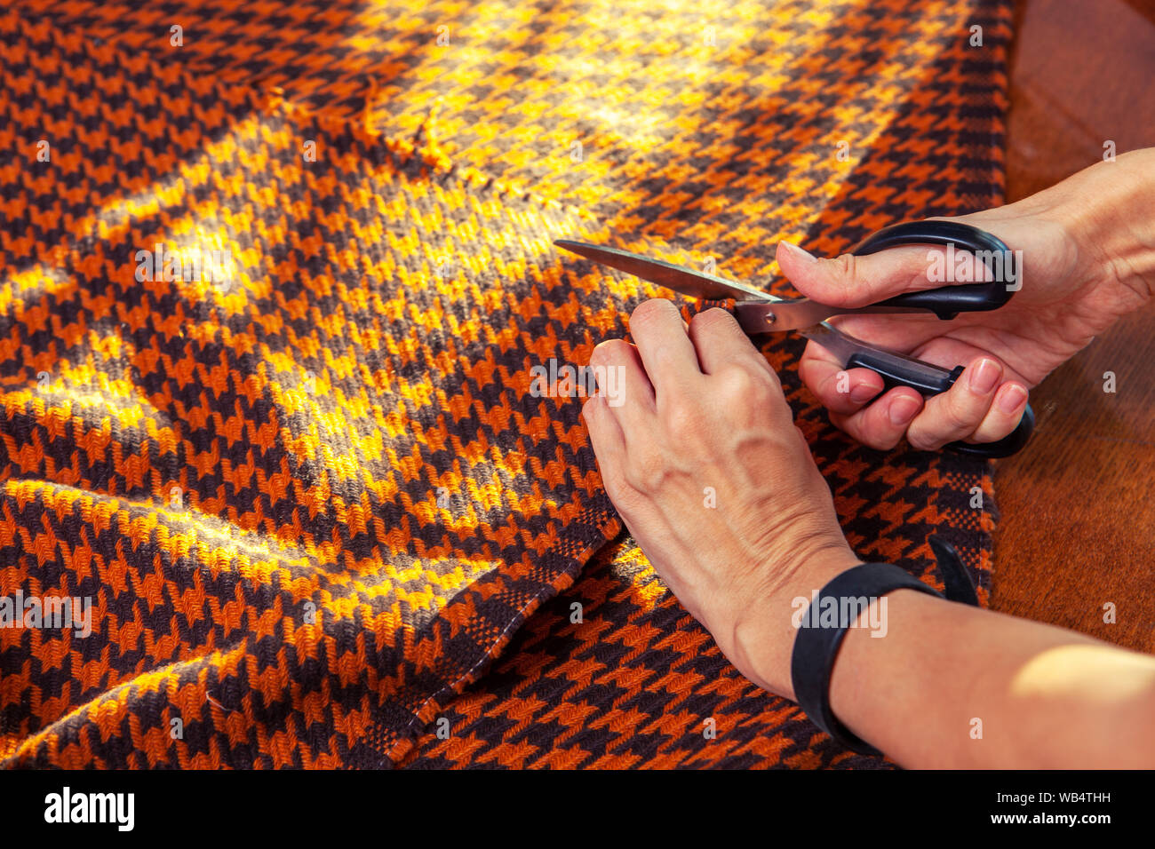 Young woman working in a sewing studio: cutting fabric with scissors ...