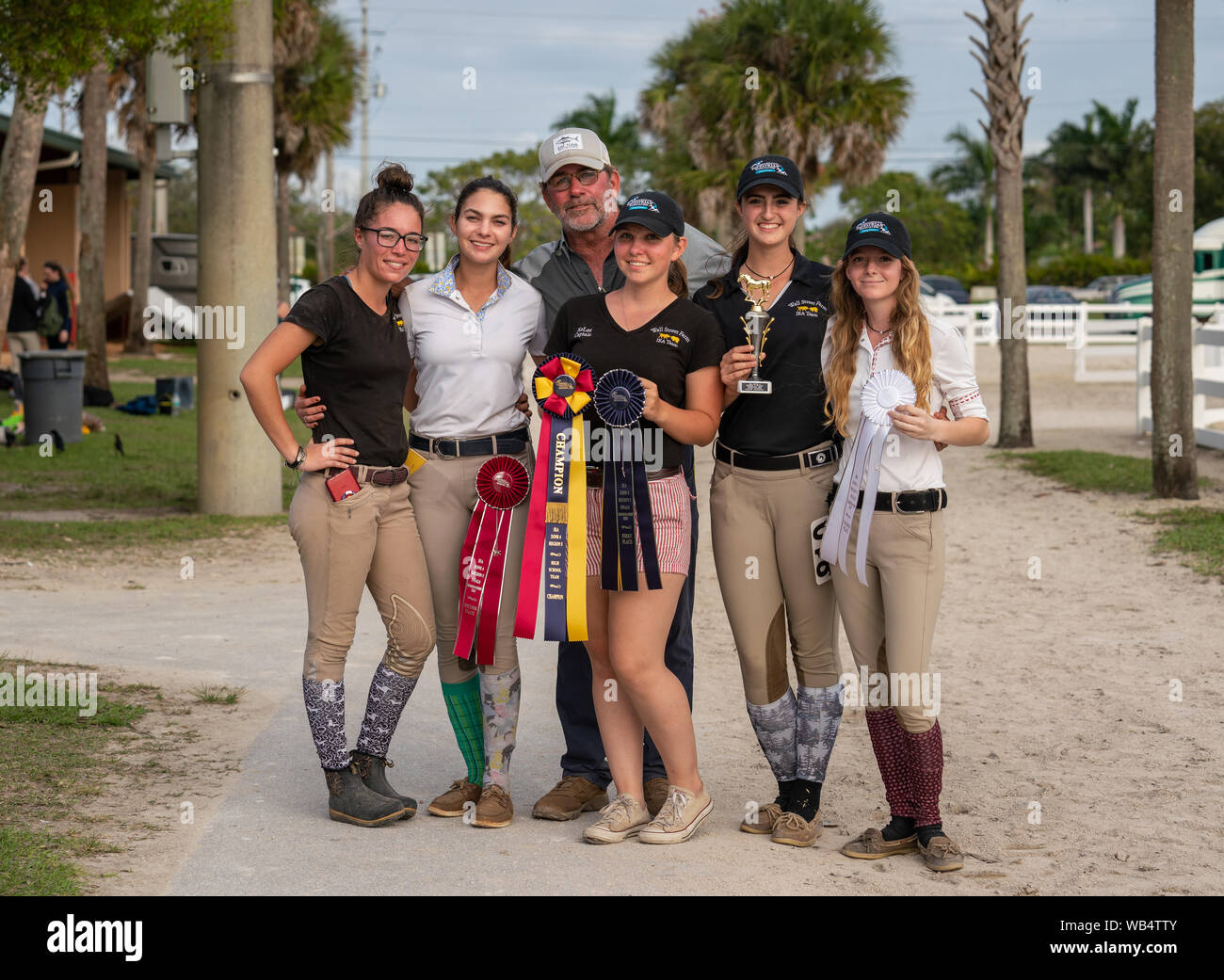 Male equestrian coach and his female student riders are holding ribbons ...