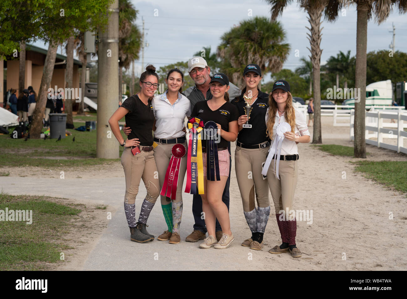 Male equestrian coach and his female student riders are holding ribbons ...