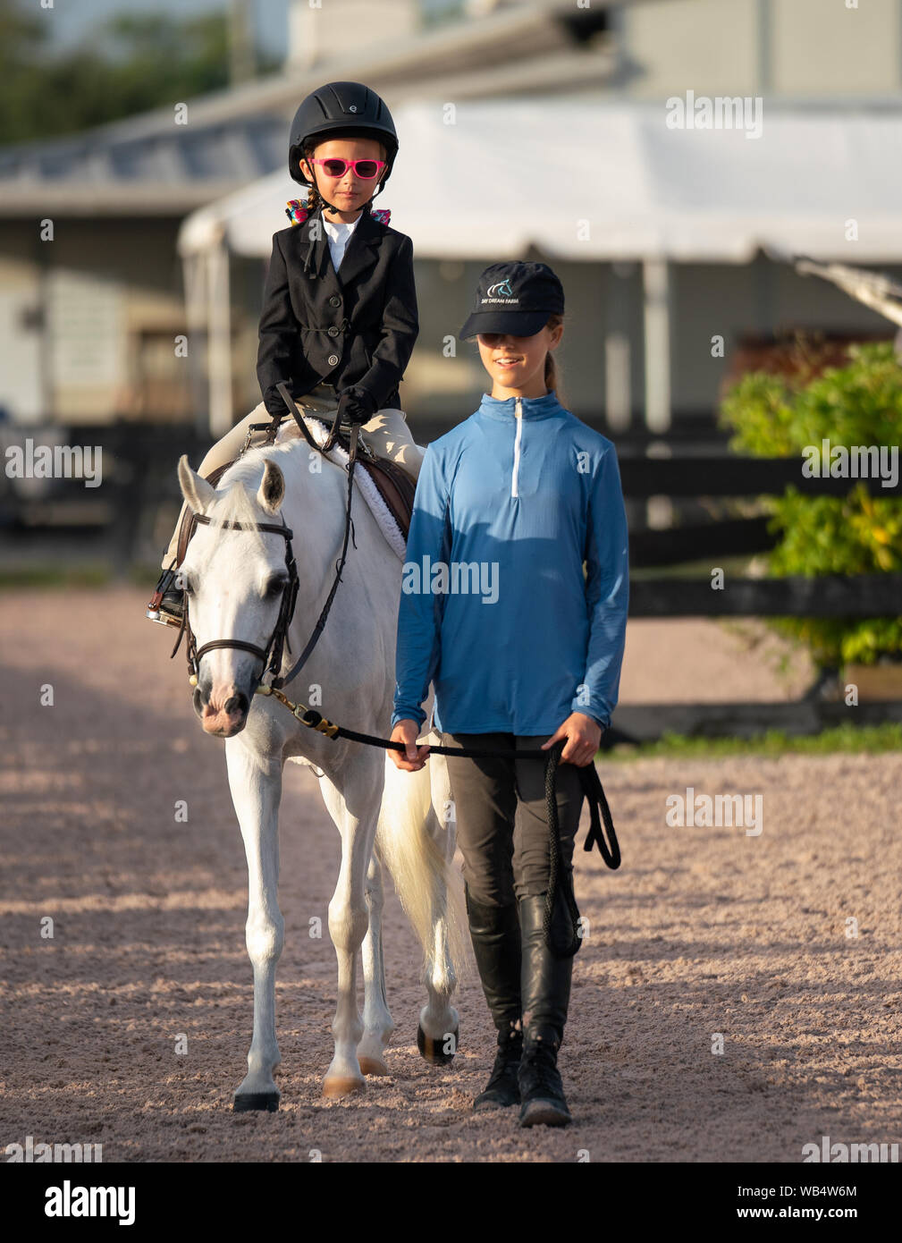 A young equestrian on a white pony is lead by an older equestrian ...