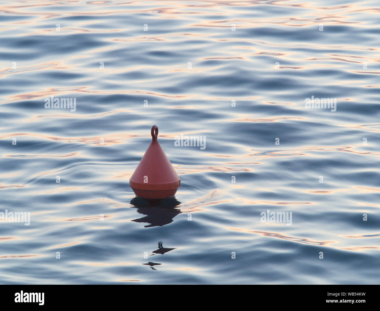 orange plastic buoy floating in calm dark ocean water at sunset. The ...