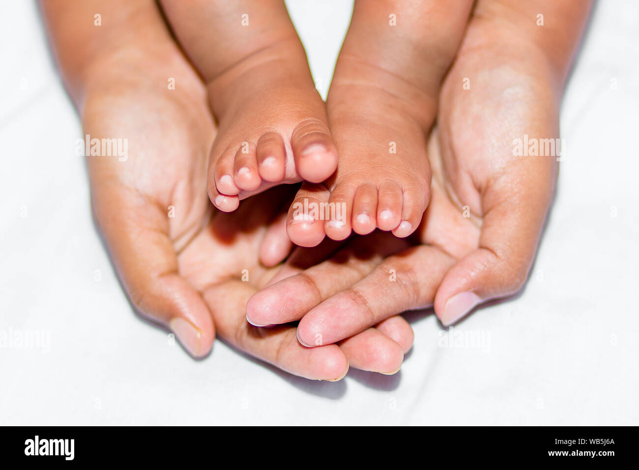 The soft legs of a baby placed on the palm of the mother's two hands on ...