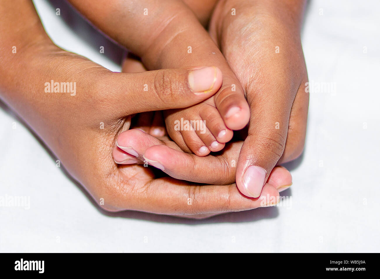 The soft legs of a baby placed on the palm of the mother's two hands on ...