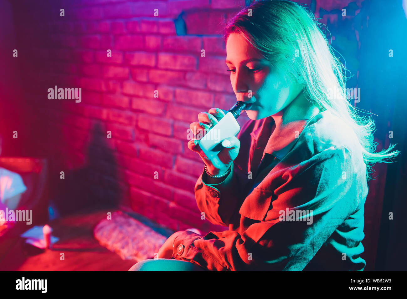 woman smokes a e-cigarette lying on the bed in the room. Smoker's ...