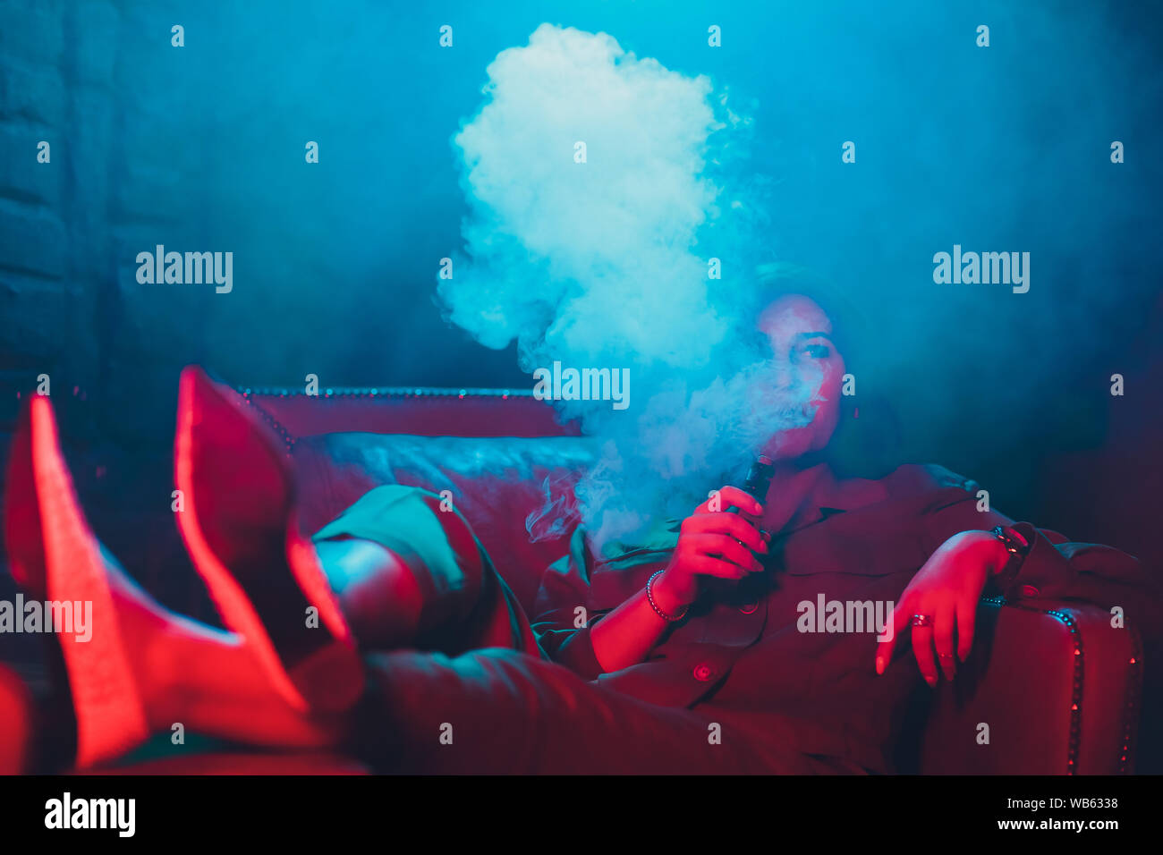 woman smokes a e-cigarette lying on the bed in the room. Smoker's ...