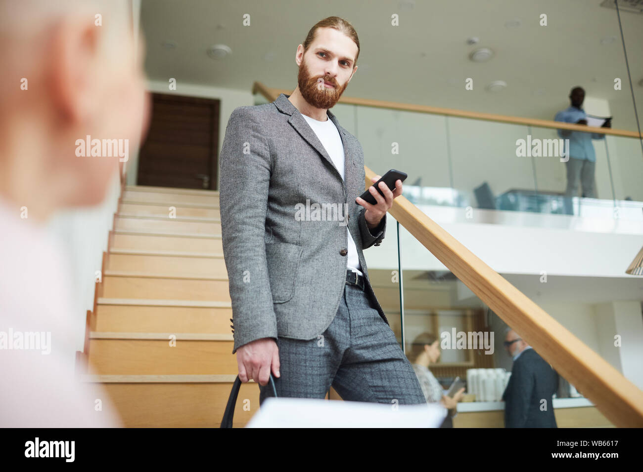 Portrait of handsome young man wearing suit coming down stairs holding ...