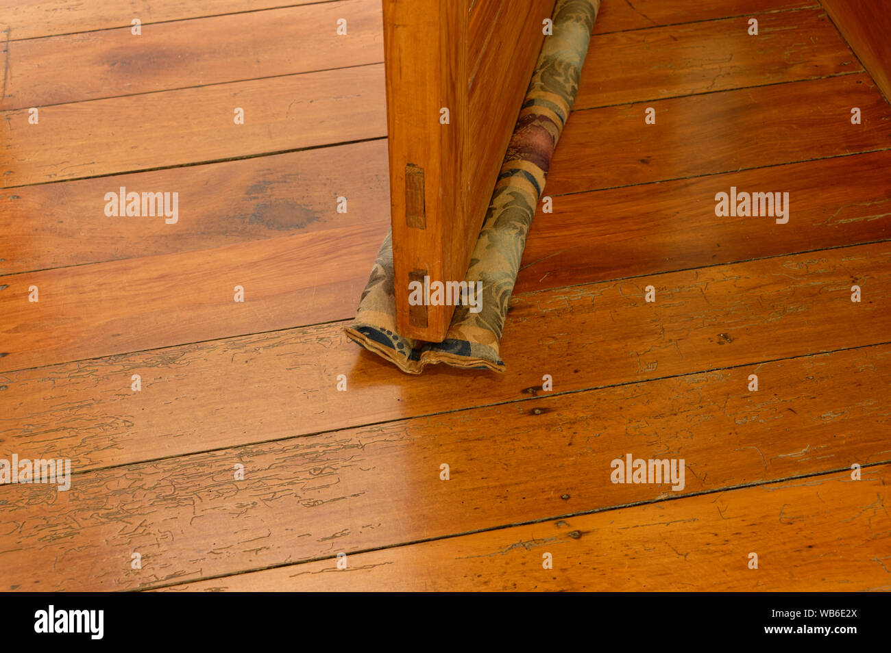A double draft stopper made from fabric slides under a wooden door and ...