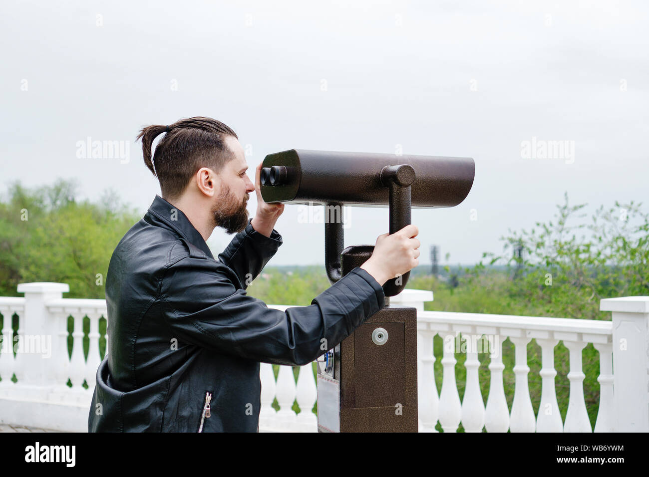 Modern stylish man looking in stationary binoculars from the ...
