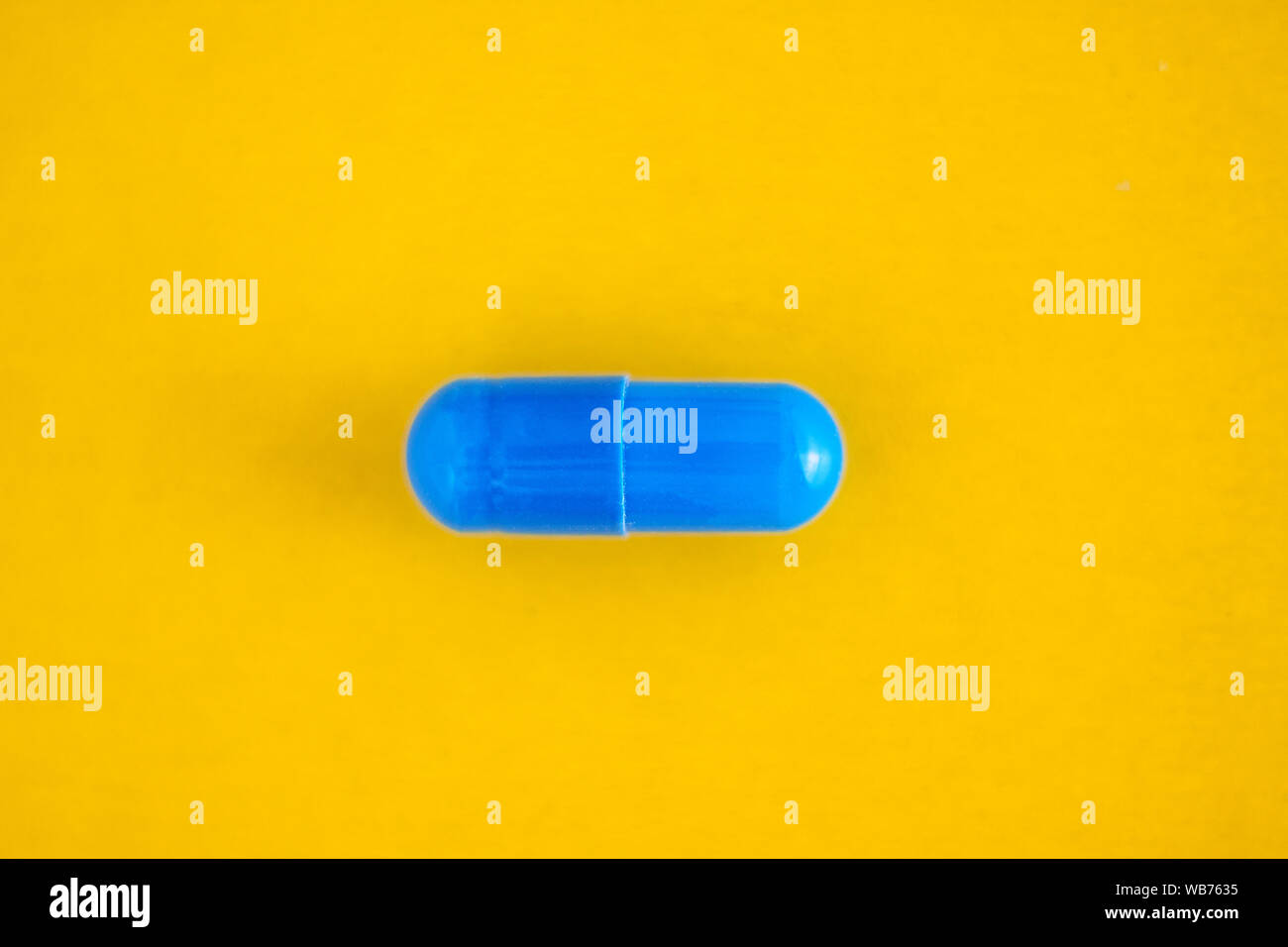 one blue pill capsule isolated on yellow background, close-up, top view ...