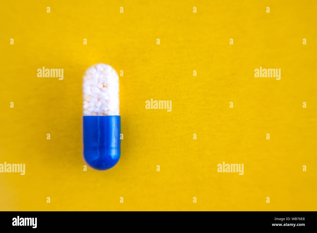 one blue pill capsule isolated on yellow background, close-up, top view ...