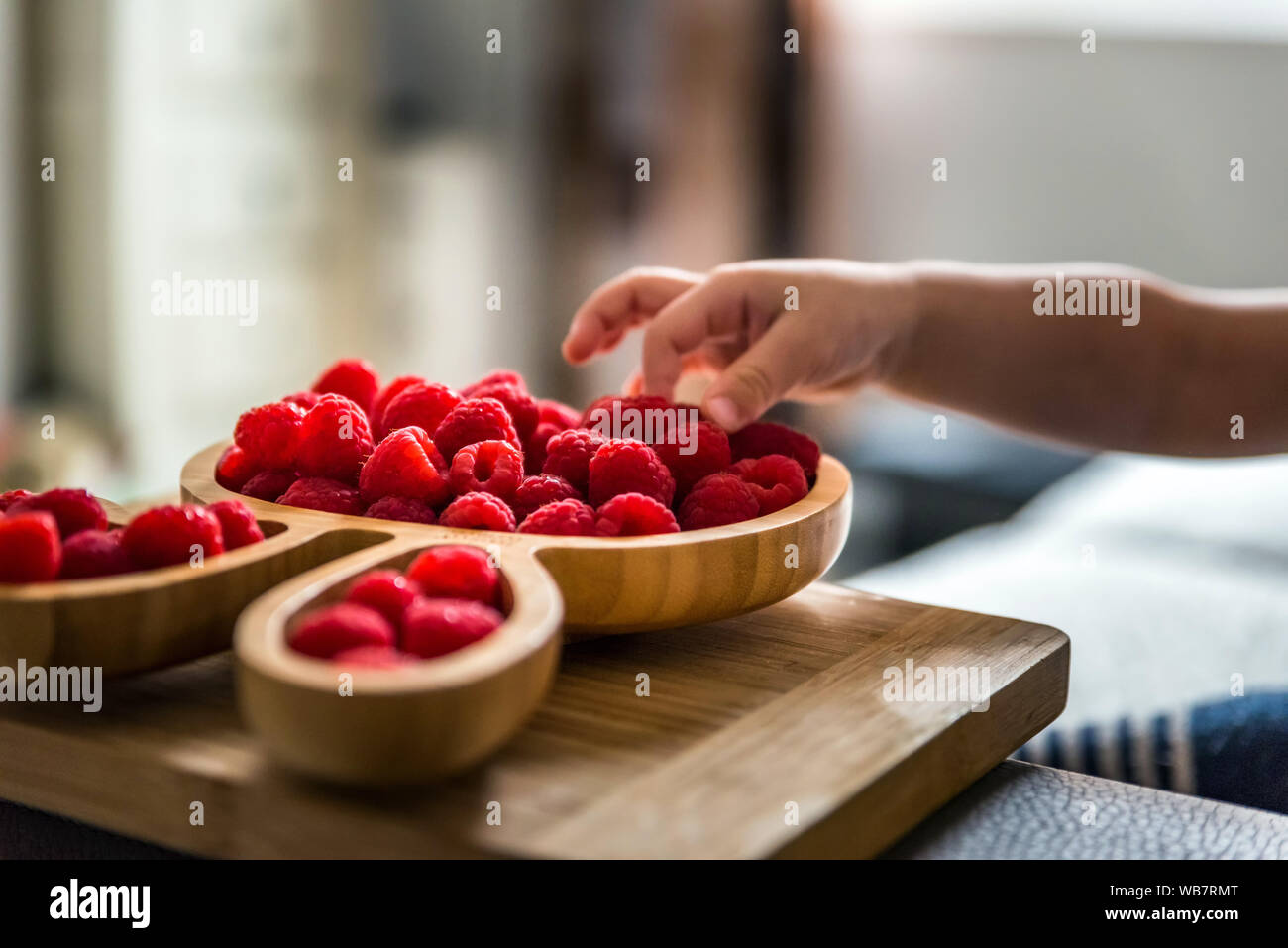 baby boy hands touch and take raw fresh raspberries on wooden bamboo ...