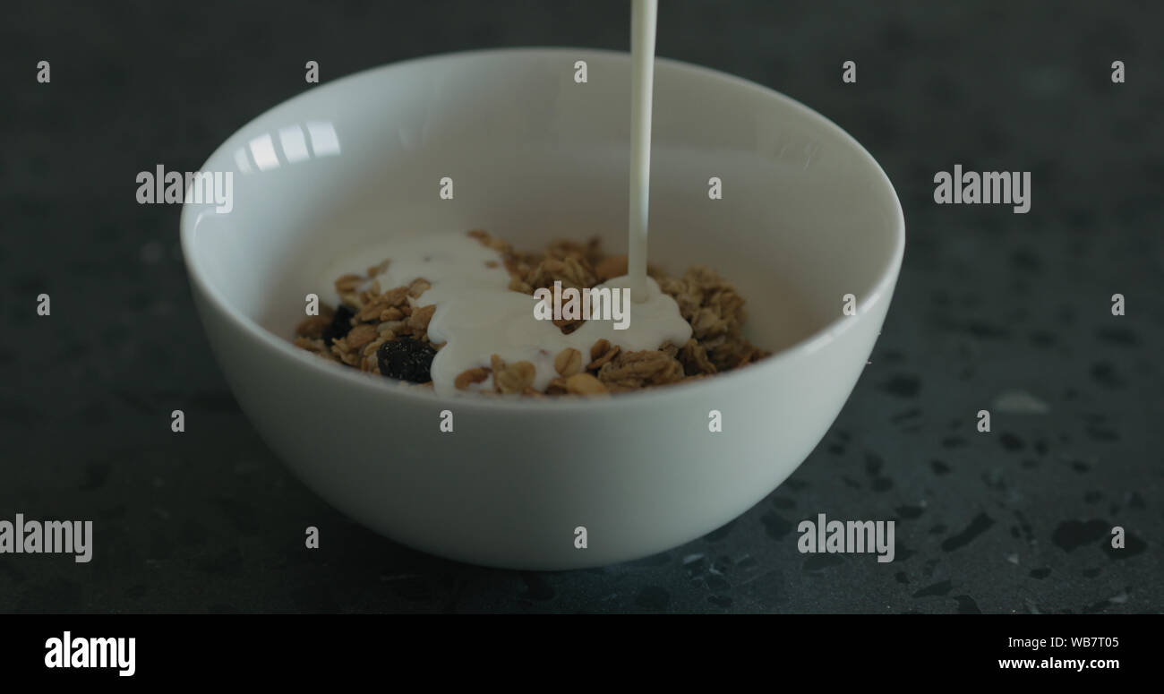 pouring yogurt into bowl with cereal muesli with nuts and raisins, wide ...
