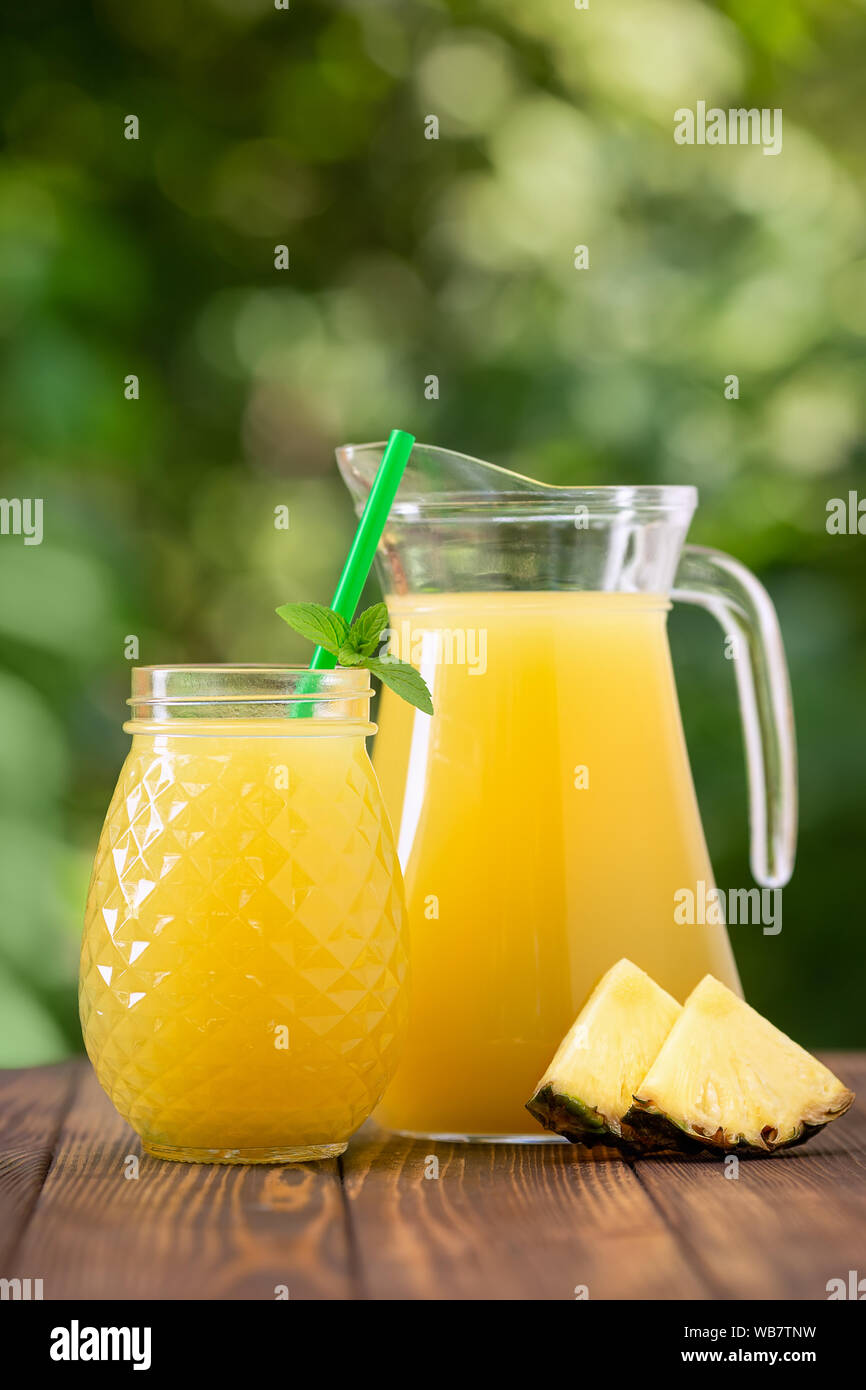 fresh pineapple juice in glass jar and jug on wooden table outdoors. Summer refreshing drink ...