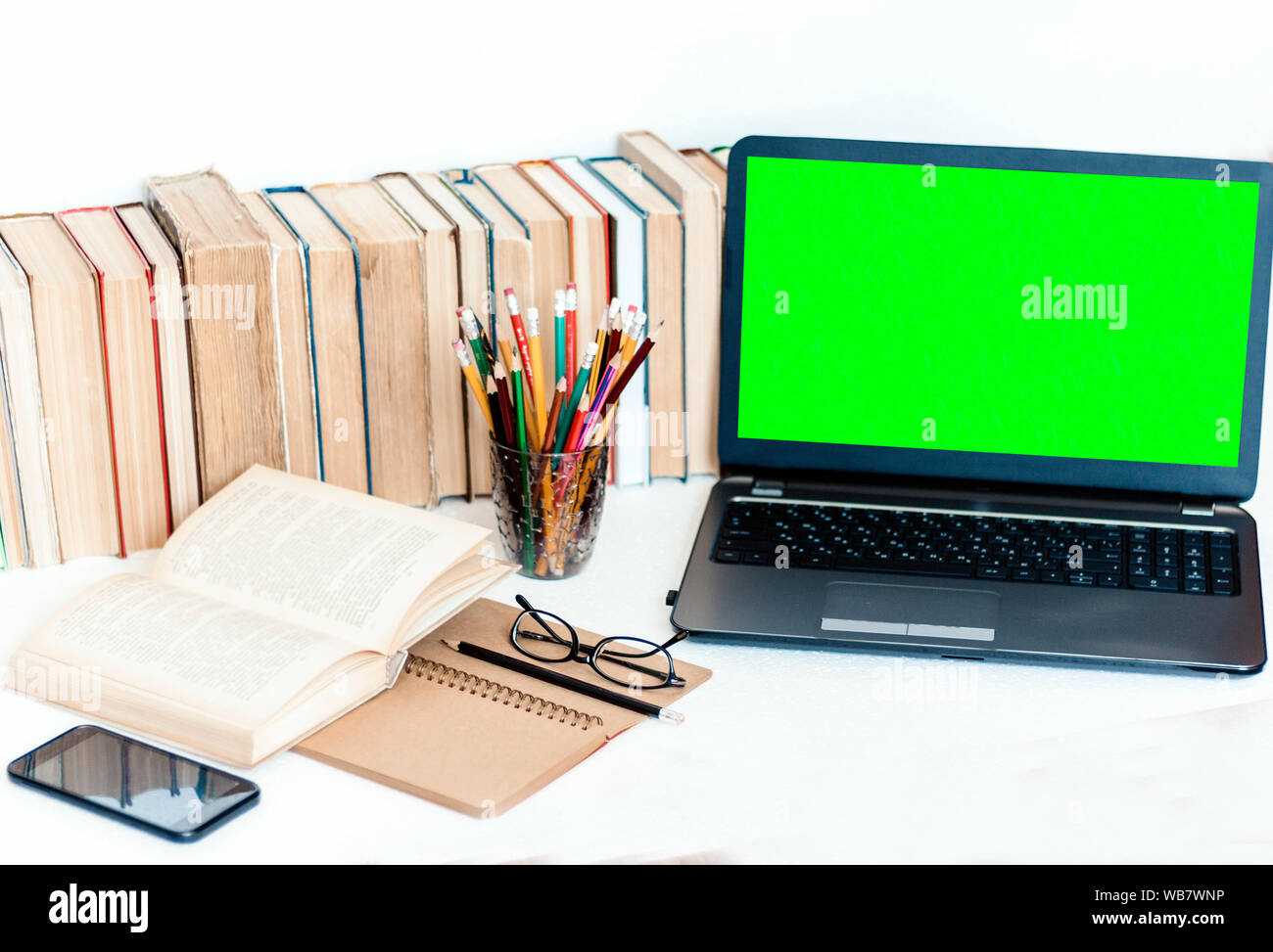Green screen laptop, pile if books, notebook, smartphone, glasses and ...