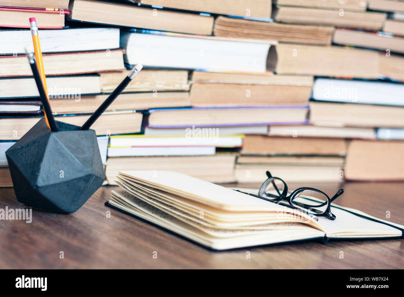 Stack of old book, pens and pencils in holder, open notebook and ...