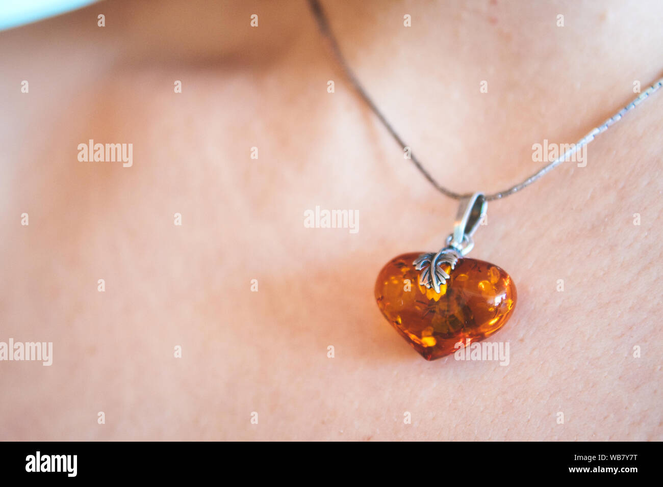 A heart shaped amber pendant worn around the neck of a young woman ...