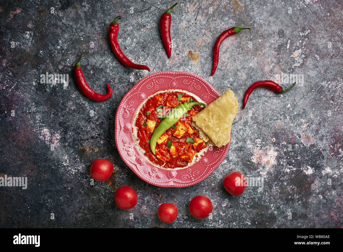 Paneer Makhani in pink plate decorated with tomatoes and chilli on dark ...