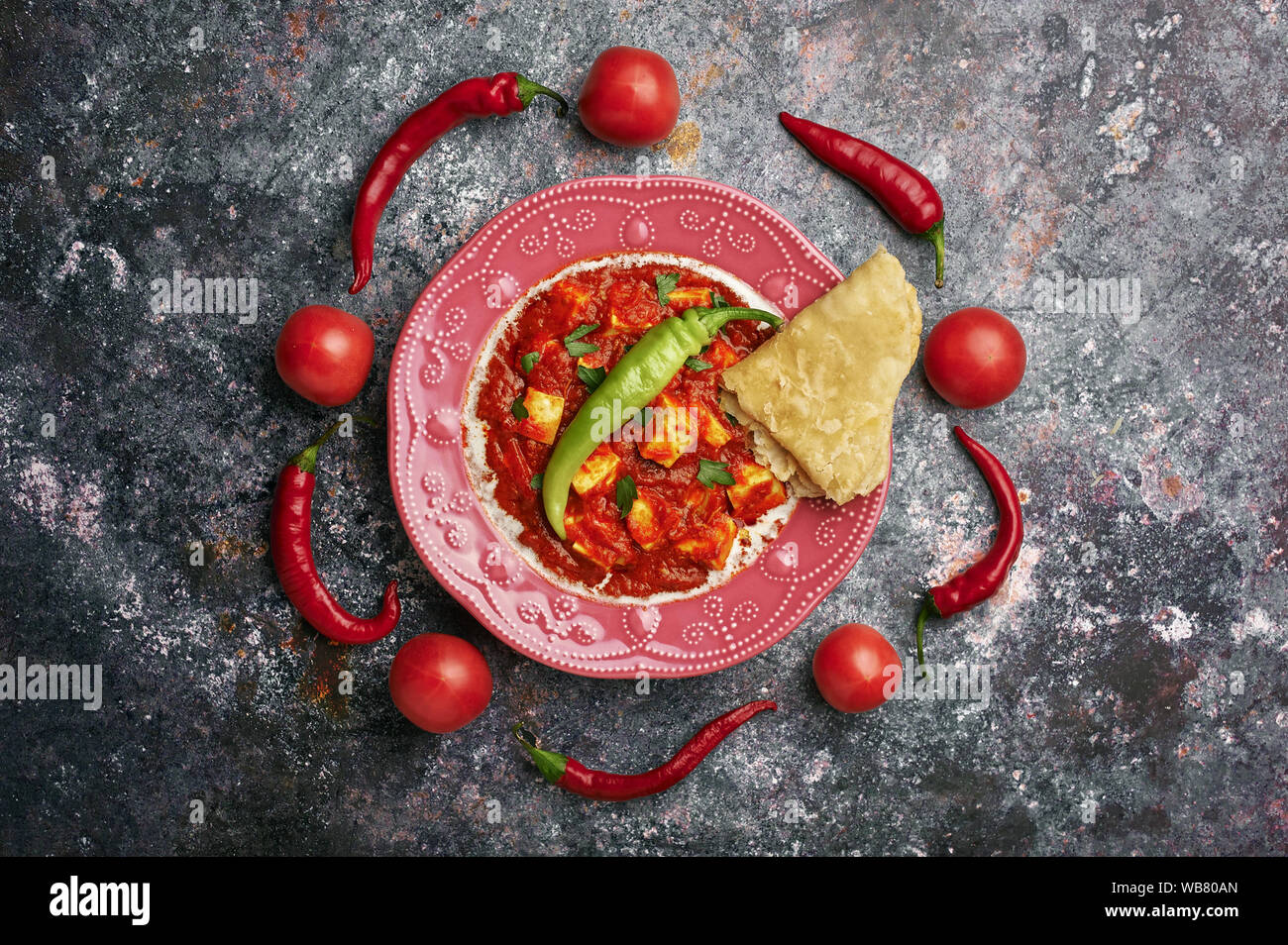 Paneer Makhani in pink plate decorated with tomatoes and chilli on dark ...
