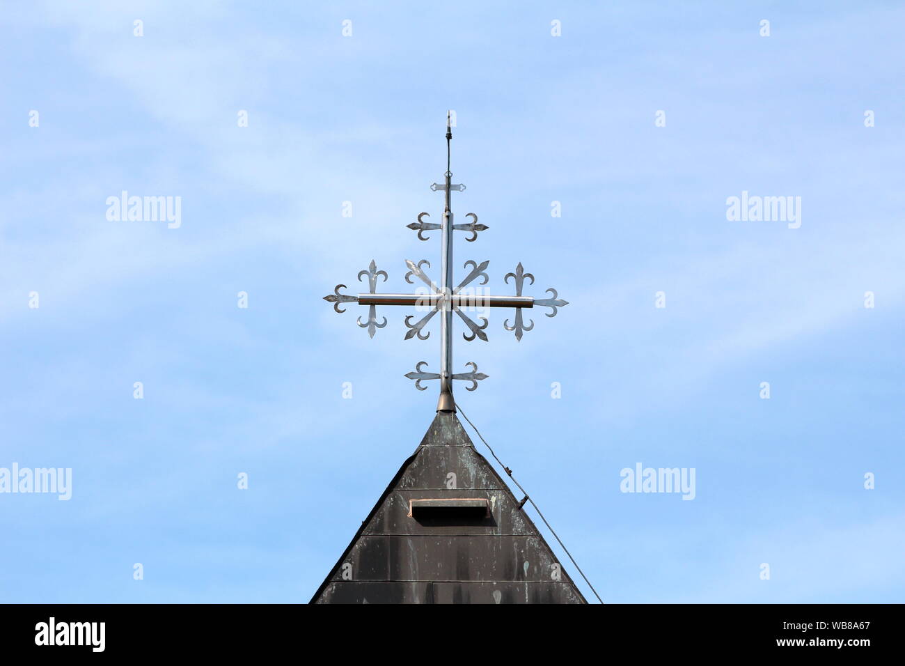 Unusual shiny metal cross on top of old local church roof surrounded ...