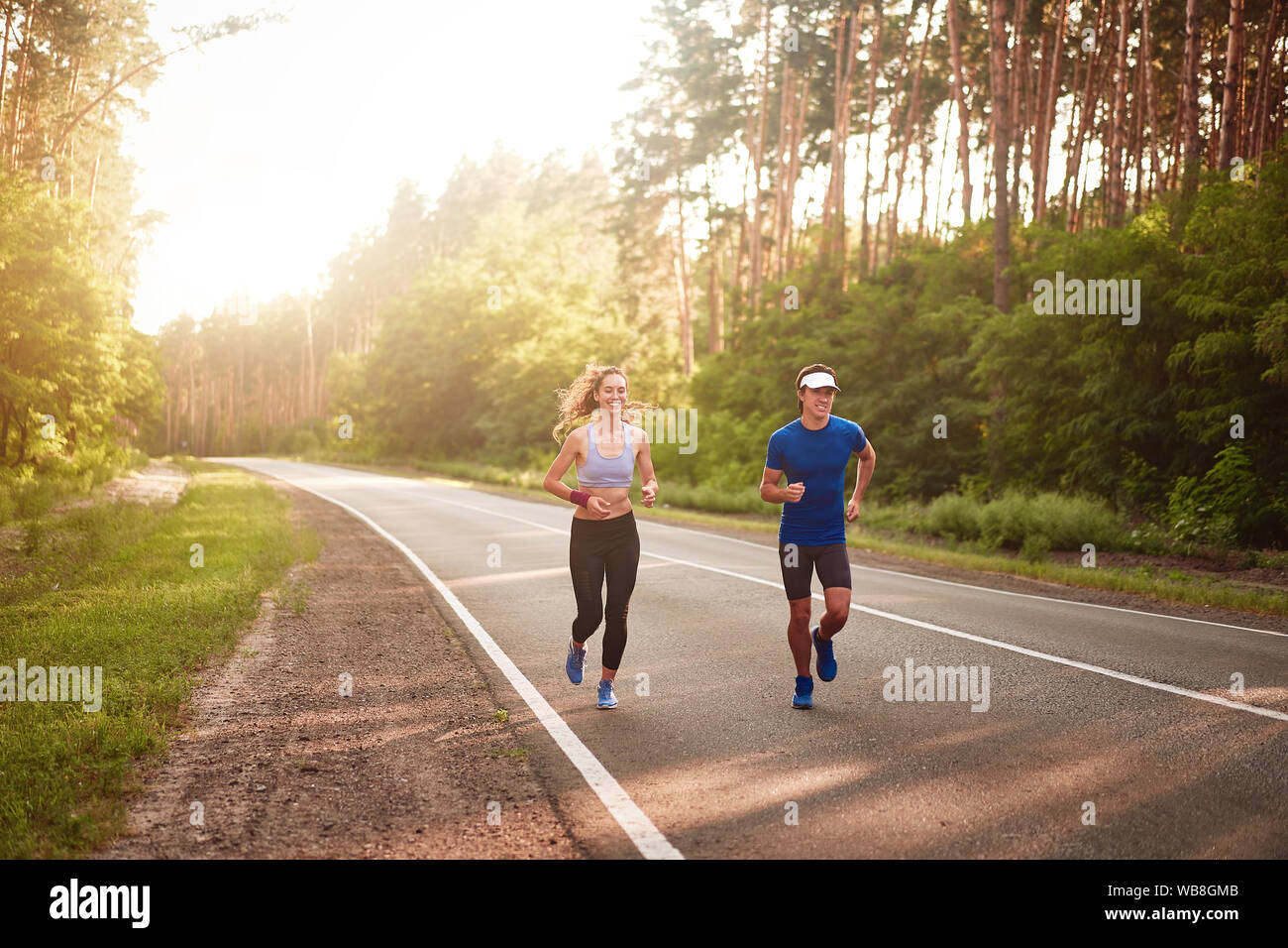 Fitness sport couple running jogging outside asphalt road pine forest ...