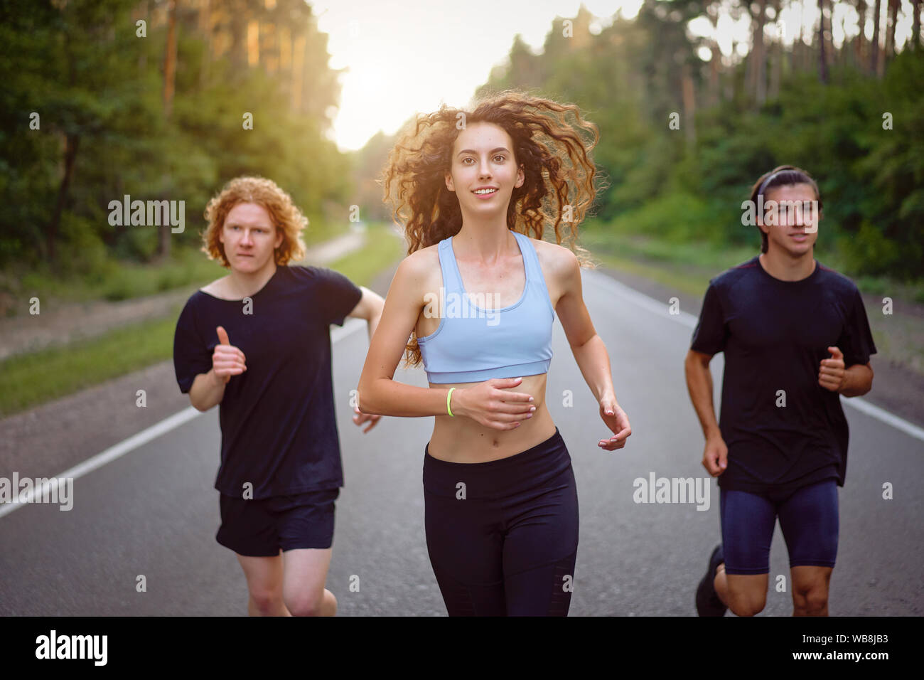 A group of three people athletes one girl and two men run on asphalt ...