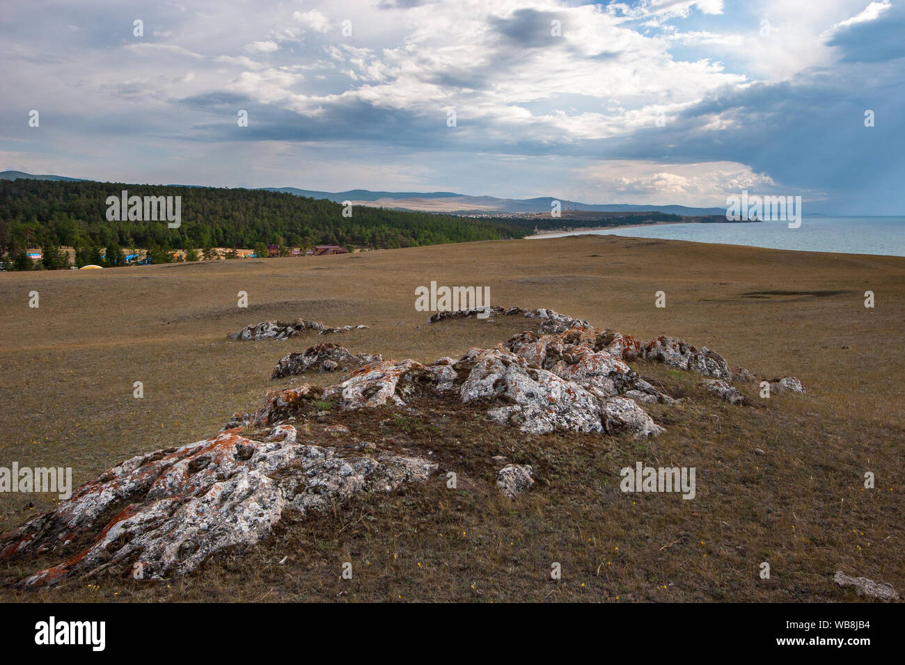 Rock in the steppe with view on lake Baikal. On the rock is red moss ...