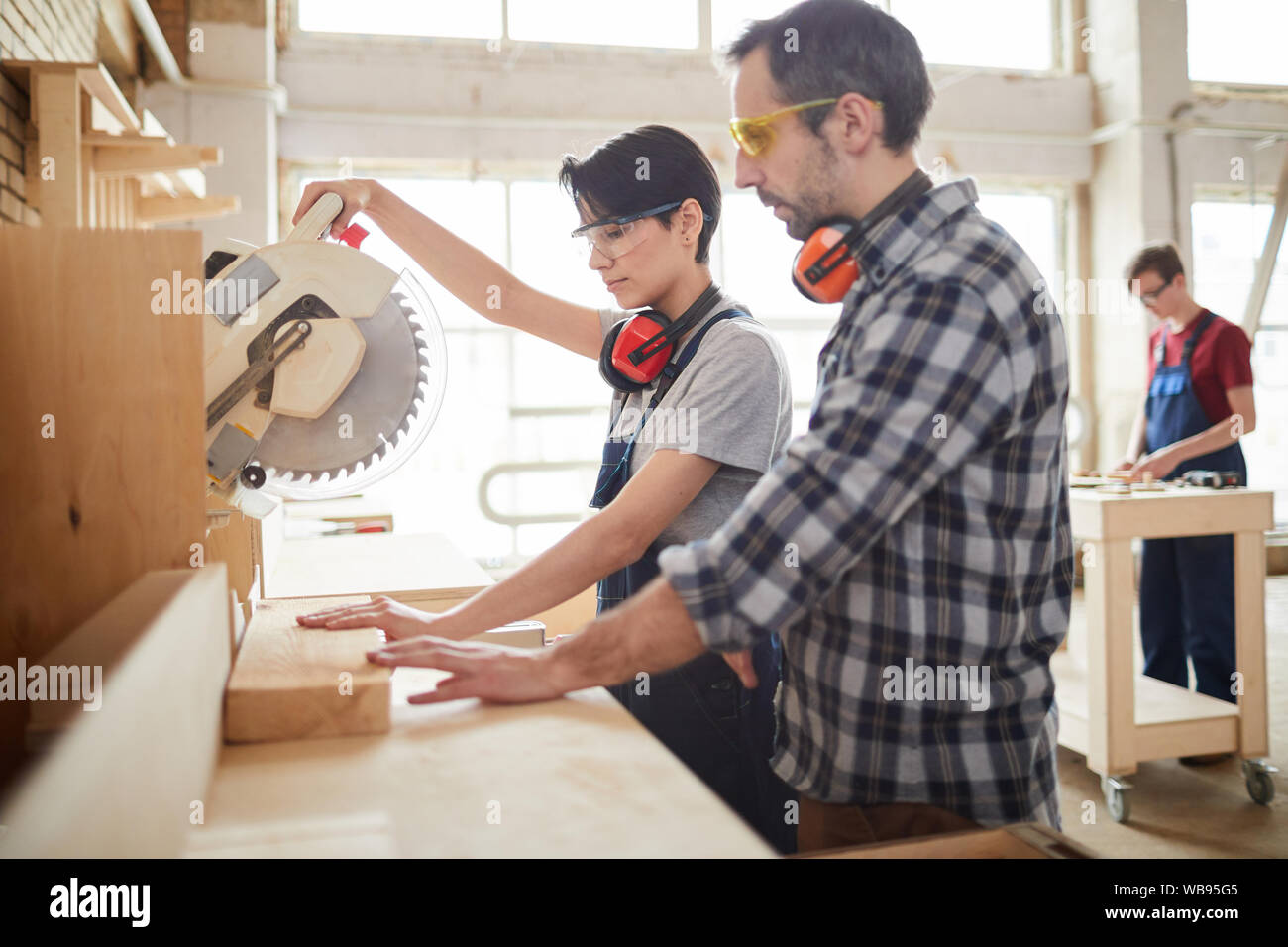 Side view portrait of mature carpenter helping young worker sawing wood ...
