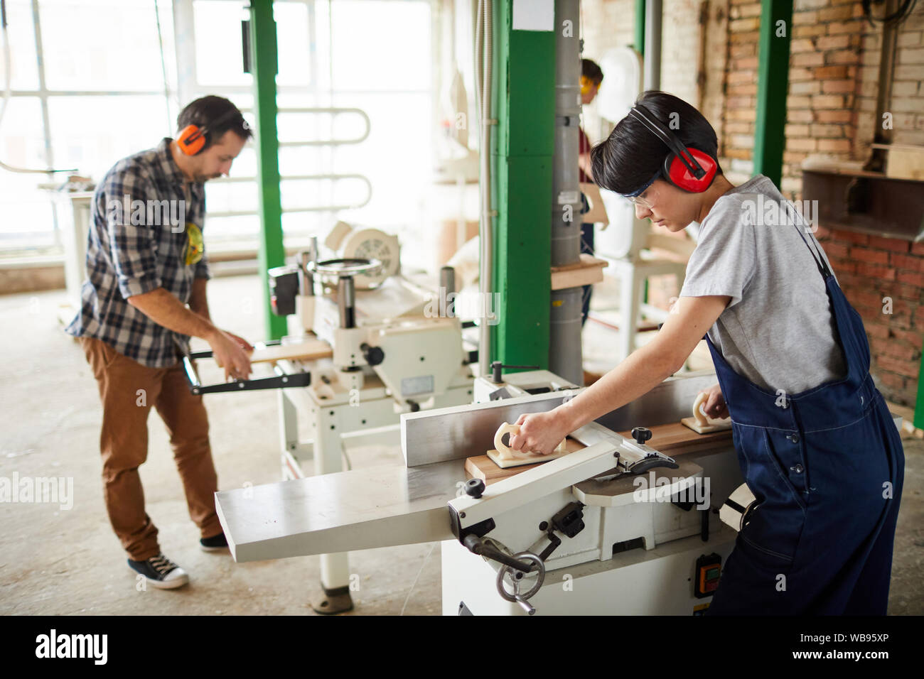 Side view portrait of carpenters using machines in joinery workshop ...