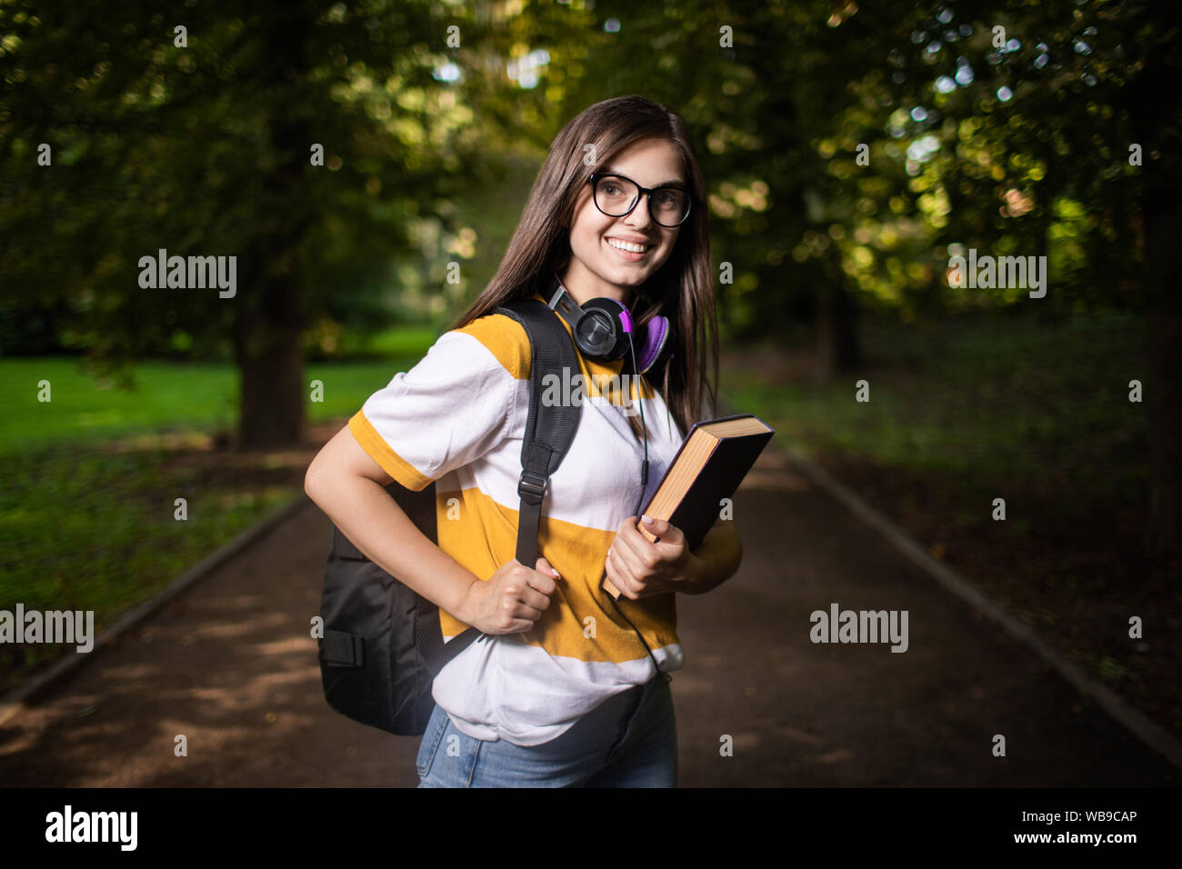 Portrait of smiling student girl standing on campus park path Stock ...