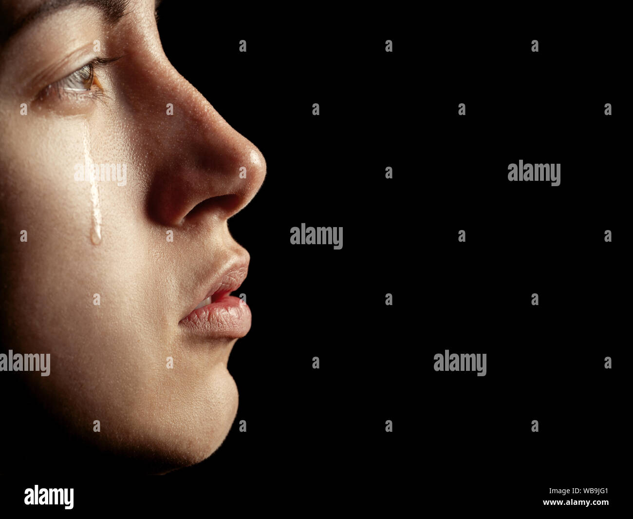 sad woman crying, looking aside on black background with copy space ...