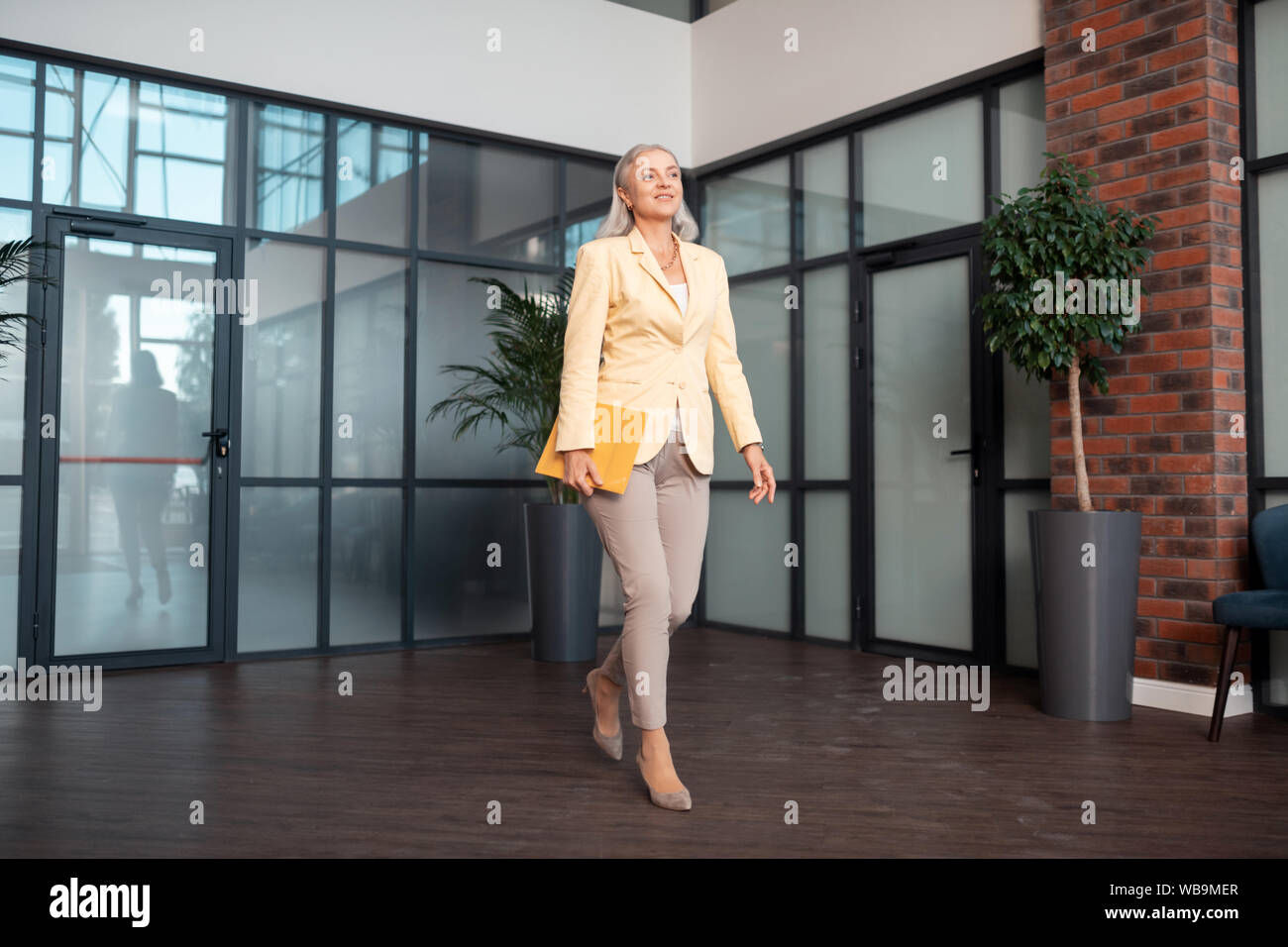 Contented senior woman in a pale yellow jacket Stock Photo - Alamy