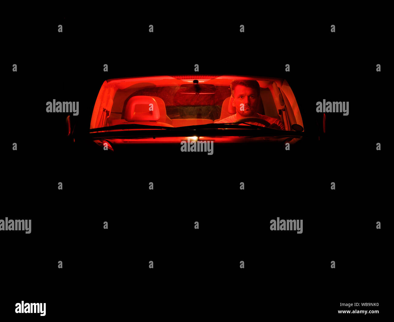A man in a car with a red light inside on a dark night. front view ...