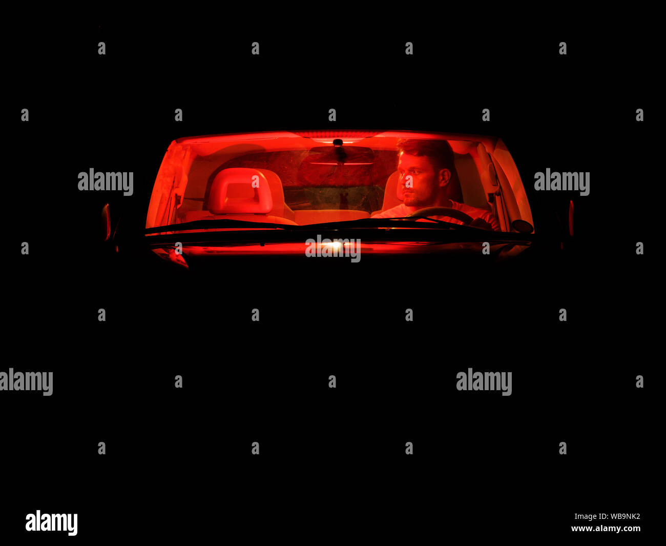 A man in a car with a red light inside on a dark night. front view ...