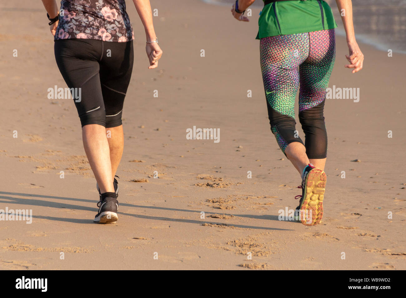 A close up back view of two women doing thier morning run on the beach ...