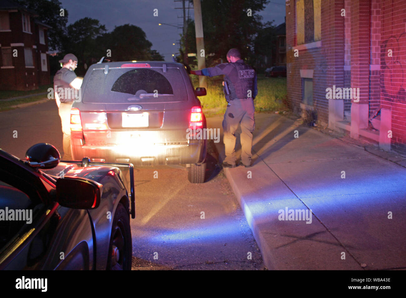 Police officers stop a vehicle at night in Detroit and speak to the ...