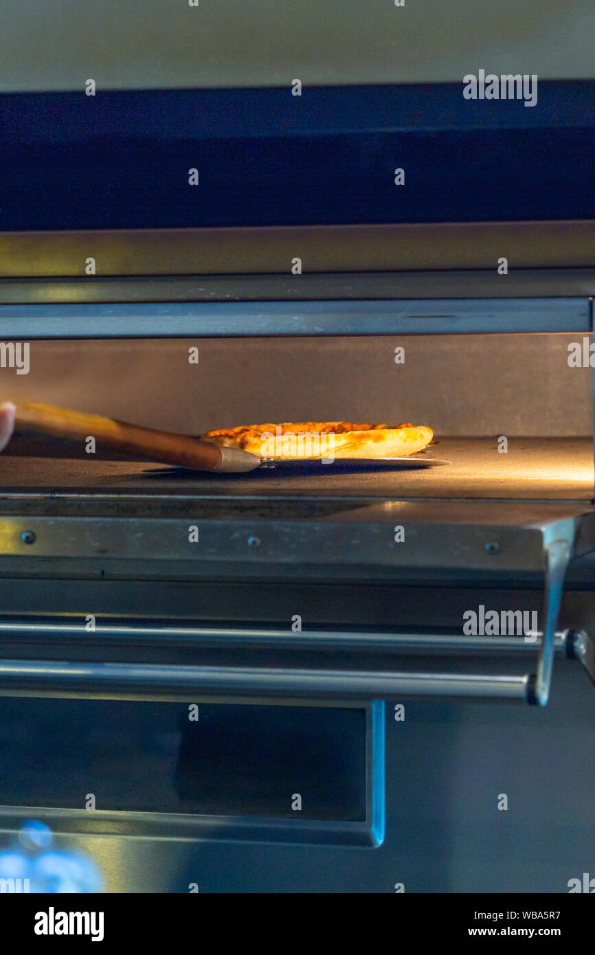 Vertical photo of baker using tool picking pizza in oven Stock Photo ...