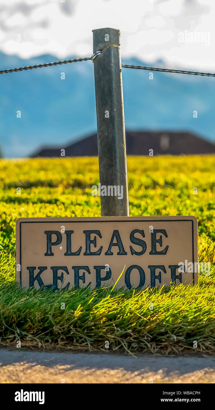 Vertical frame Please Keep Off sign against vibrant grasses and post of ...