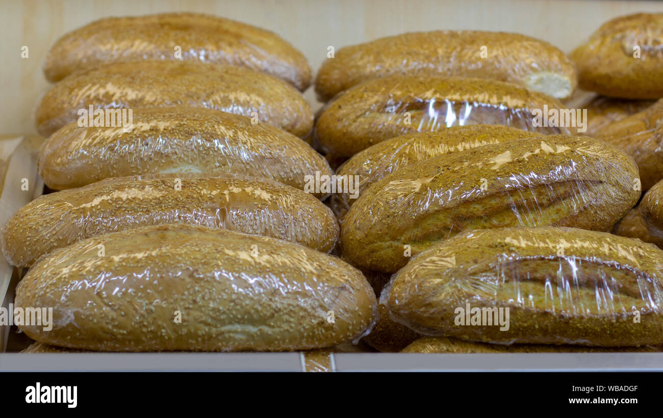 Loafs of fresh grain bread wrapped in polyethylene on a bakery counter ...