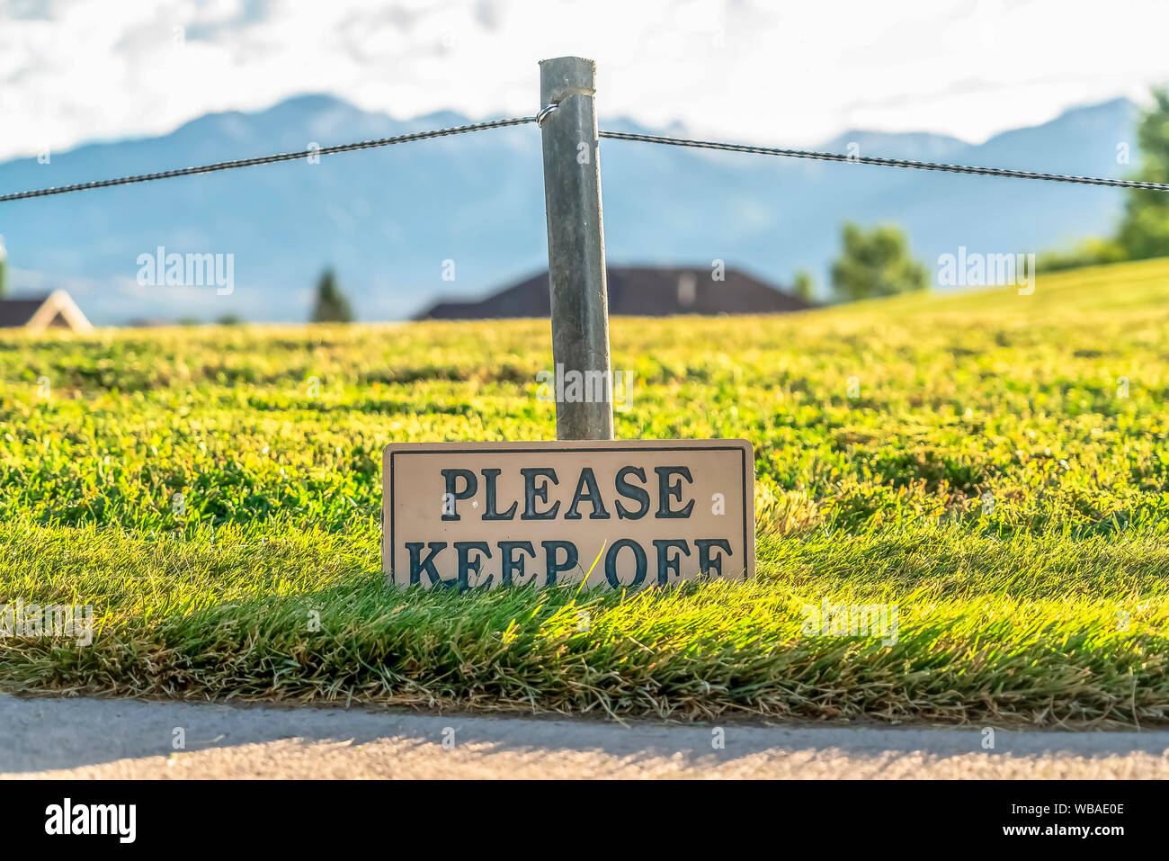 Please Keep Off sign against vibrant grasses and post of a wire fence ...