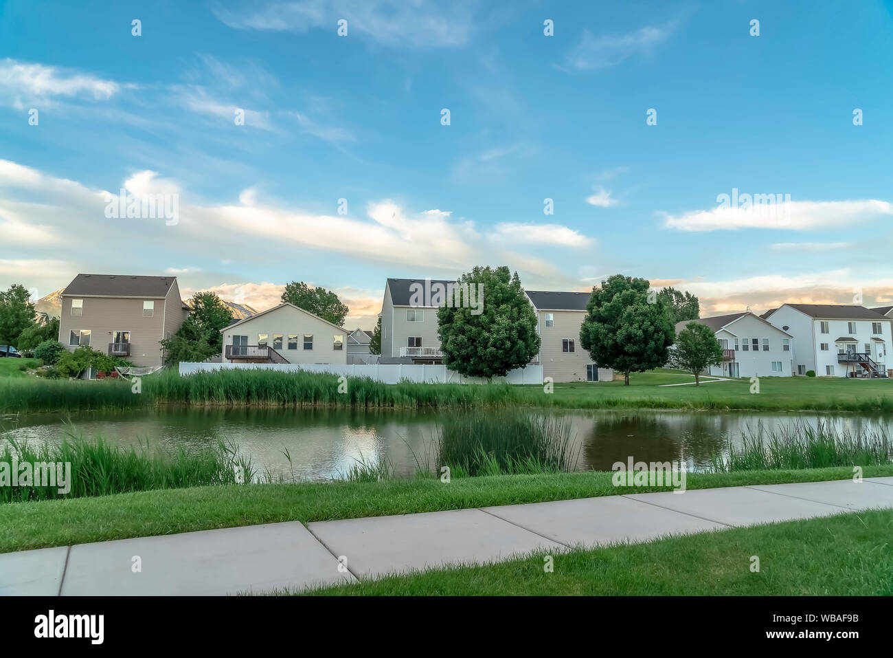 Pathway along a shiny pond on a grassy terrain with homes in the ...