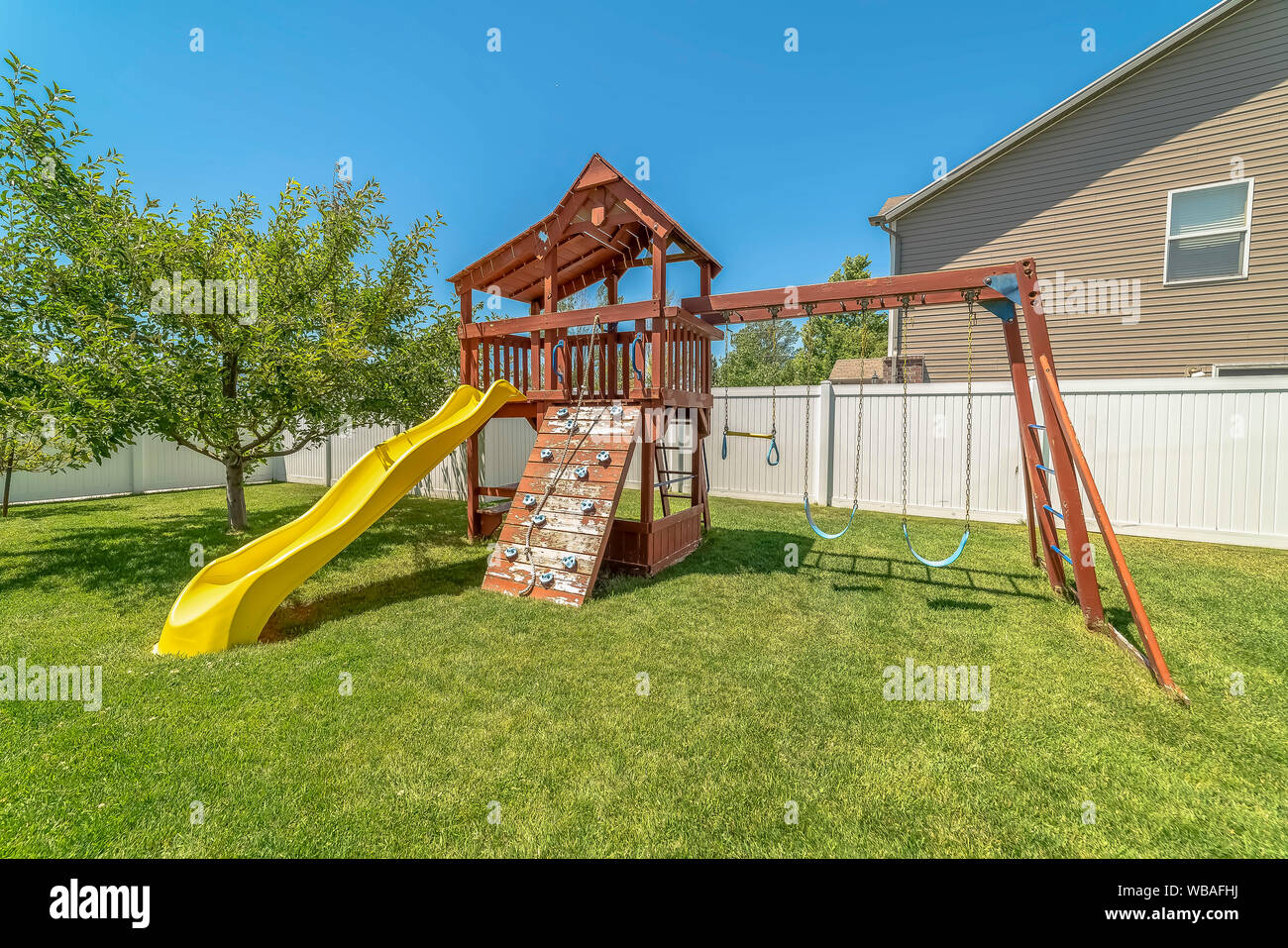 Wooden playground structure with yellow plastic slide swings and ...
